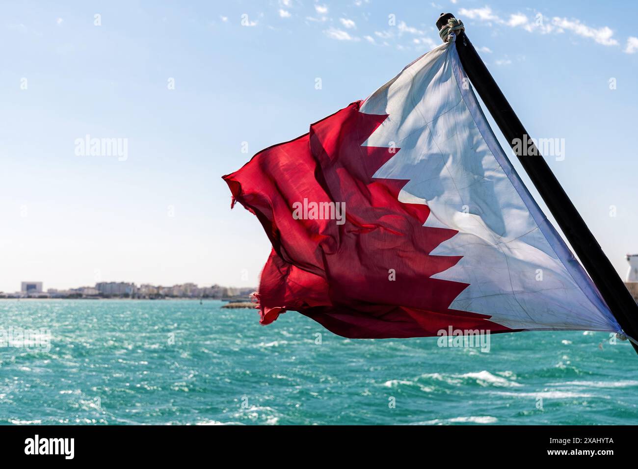 Wavy Qatar flag on the flagpole on the fast boat in the sea in front of ...
