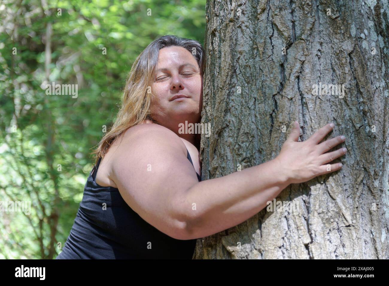 Contented young woman hugging a large tree with a blissful expression ...