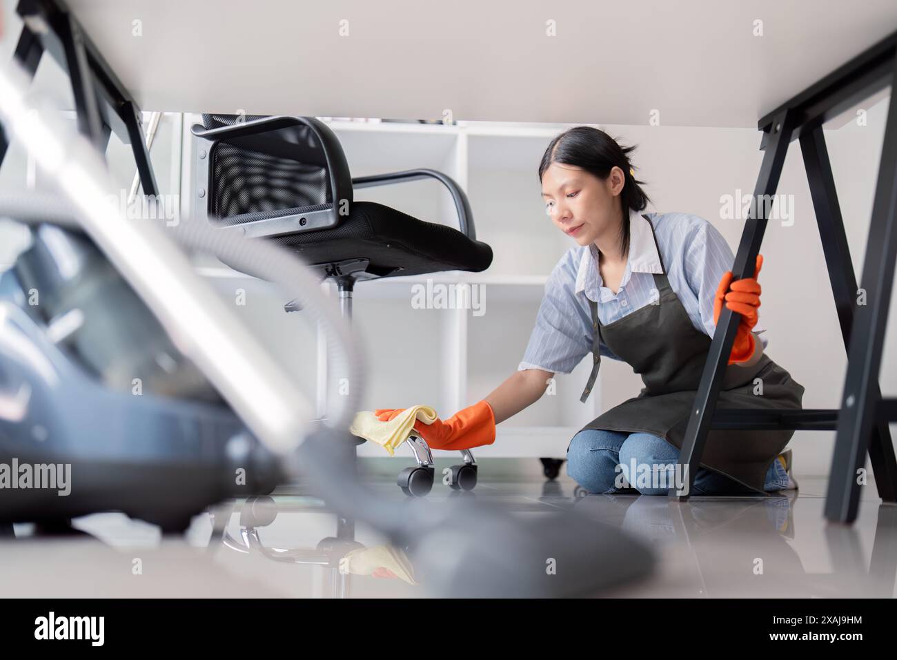 Female office cleaner wiping floor under desk with cleaning supplies ...