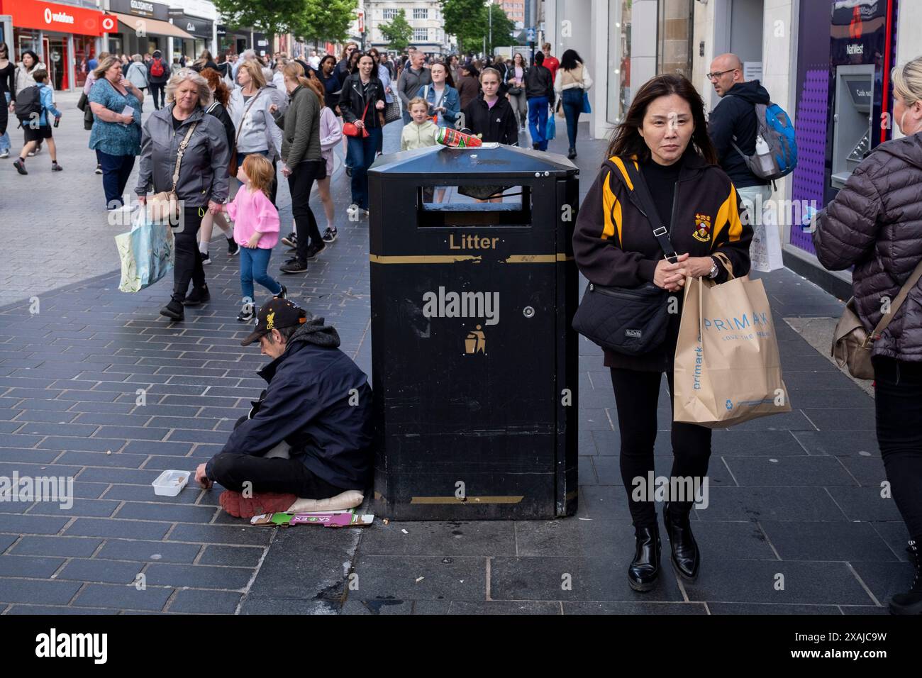 Man sitting on the pavement collecting money while people with shopping ...
