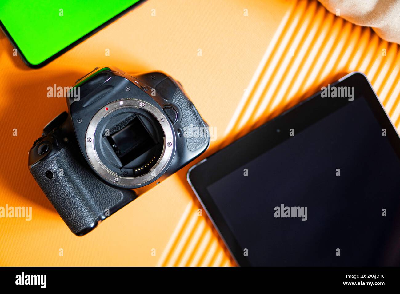 A SLR camera without a lens next to a tablet on an orange surface Stock ...