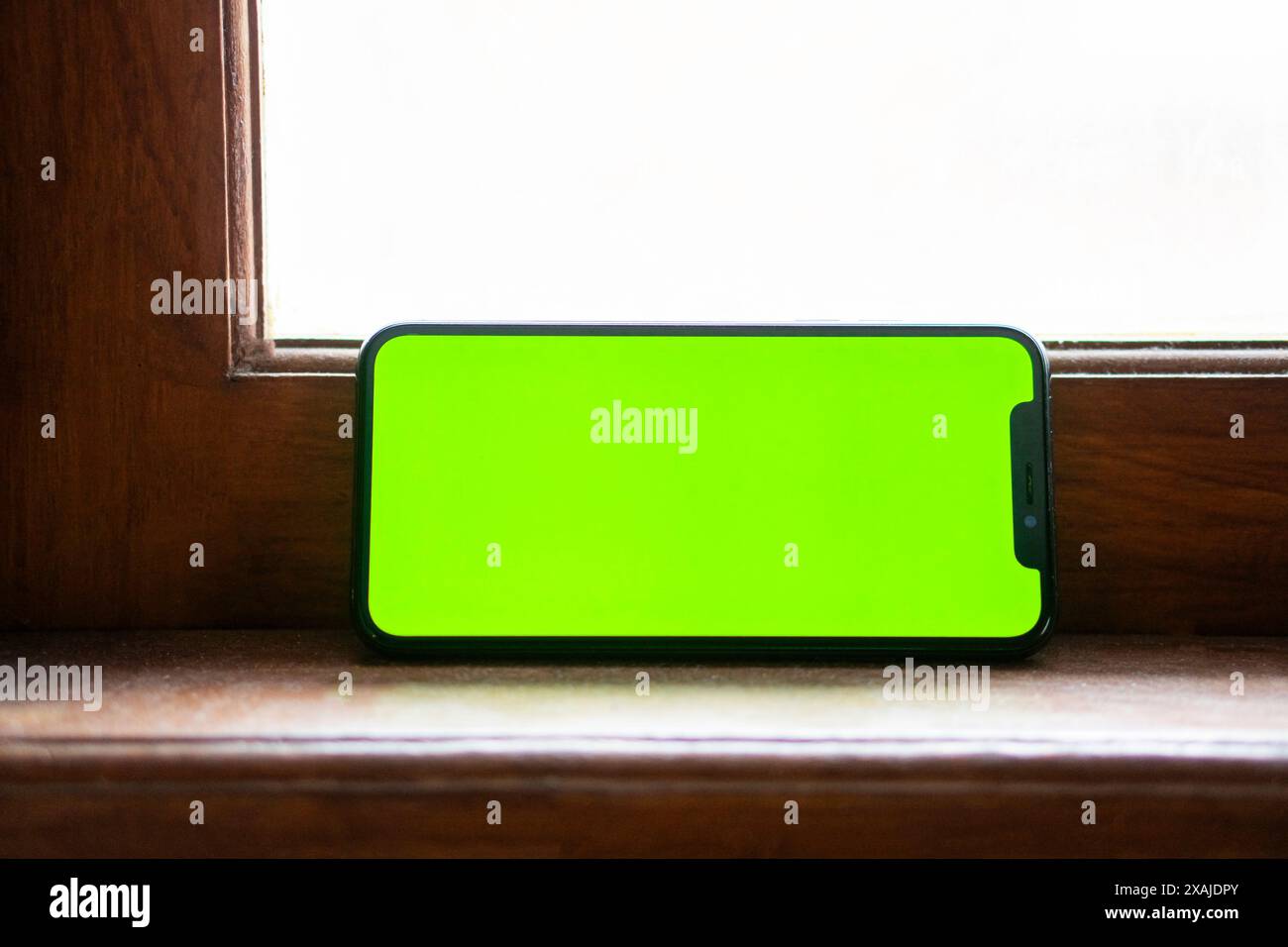 A smart phone with a green screen placed horizontally on a wooden ...