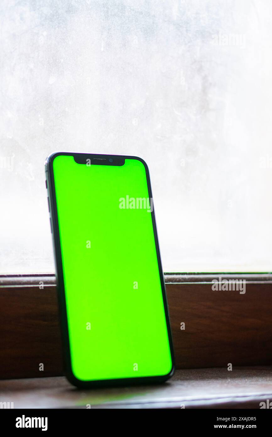A smart phone with a green screen placed on a wooden surface in front ...
