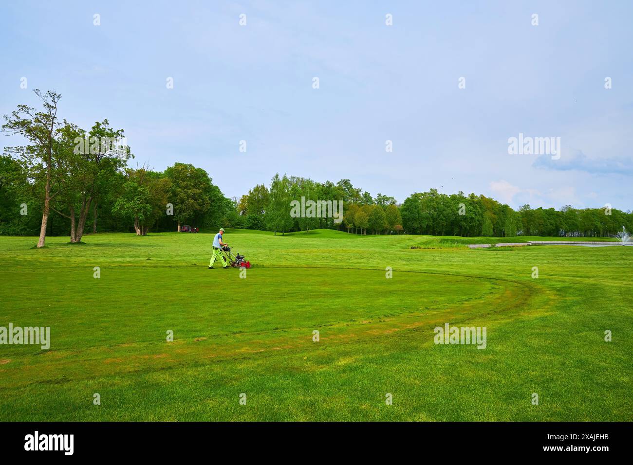 A golf course, with meticulous lawn care underway as a lawnmower trims ...