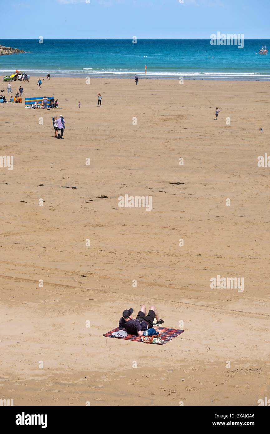 A mature male holidaymaker lying down alone on a blanket on a beach in ...