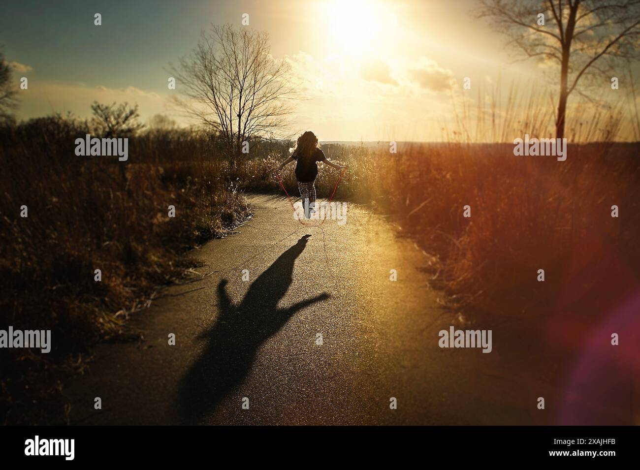 Young girl jumping rope down path near sunny field Stock Photo - Alamy