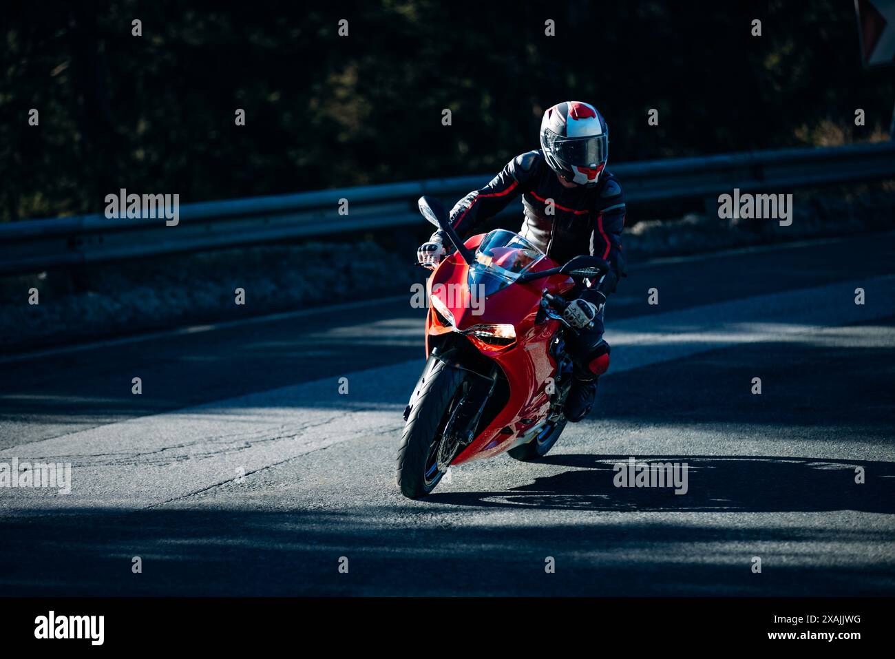 Motorcyclist leans on red racing bike in curve shadow and sunlight ...