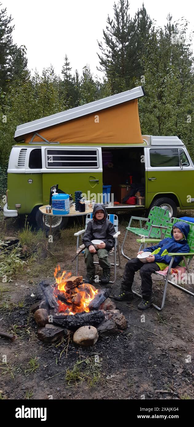 Kids enjoy campfire warmth by a vintage camper van Stock Photo - Alamy