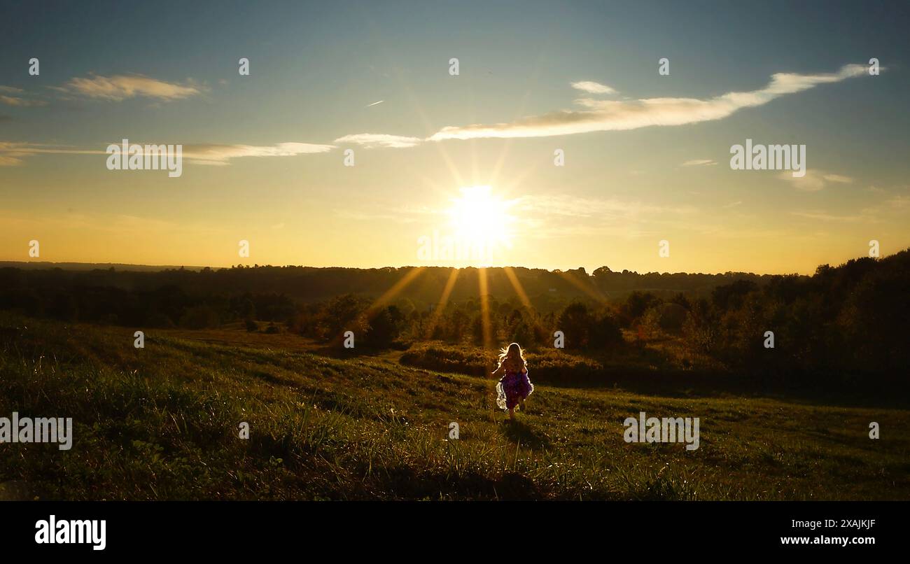 Young girl running down field into sunset under blue sky Stock Photo ...