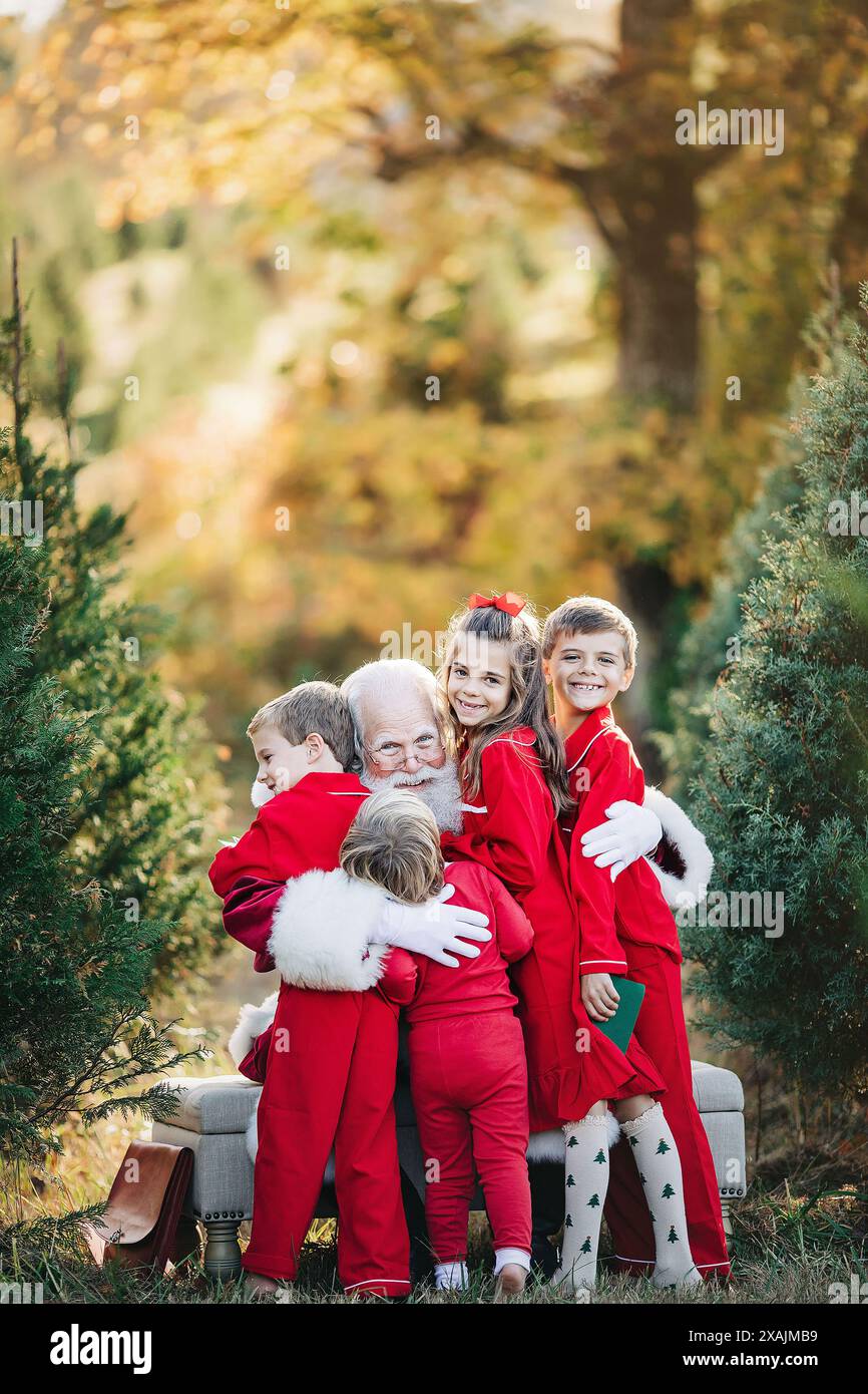 Santa hugging four children in red pajamas outdoors among trees Stock ...