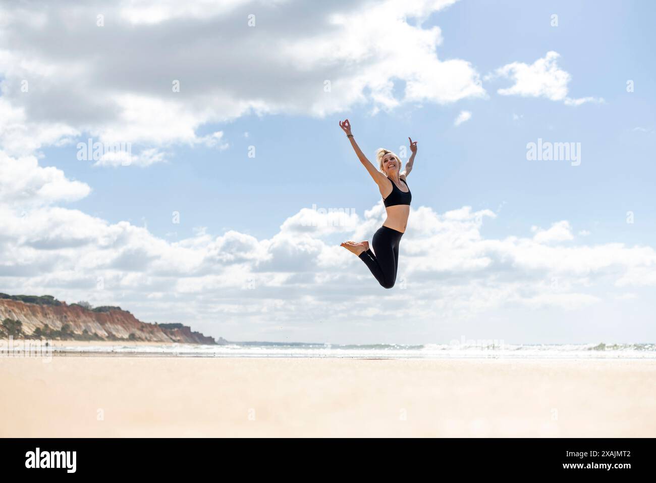 Woman taking a leap on the beach, Praia do Barranco das Belharucas, Olhos de Agua, Algarve ...