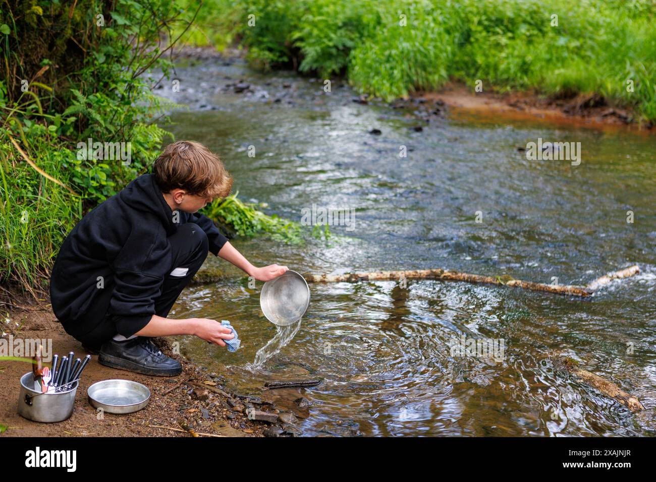 A young teenage boy washing up a few pots in the river, whilst wild ...