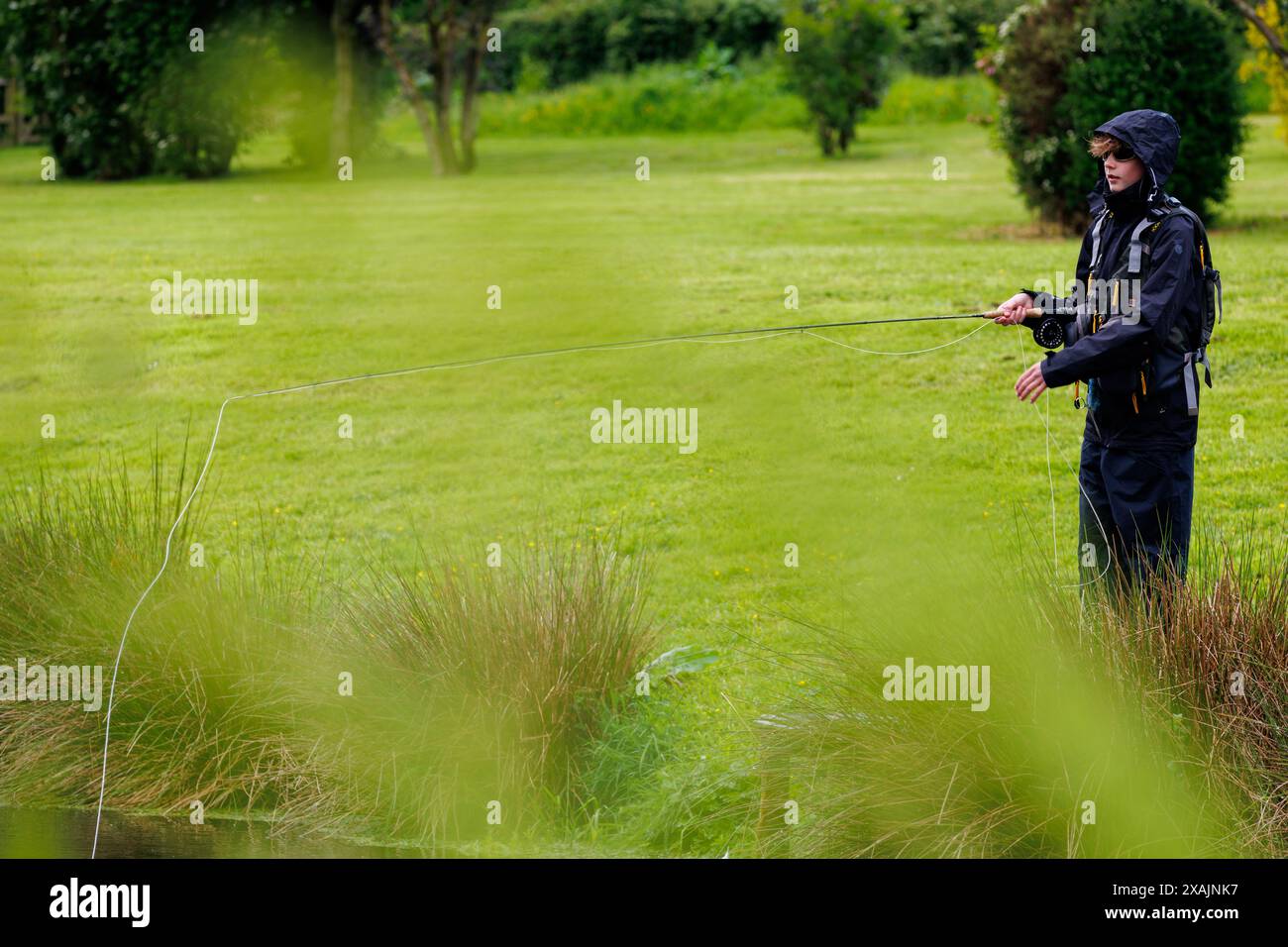 A portrait of a teenage boy in full fishing clothes with his rod over ...
