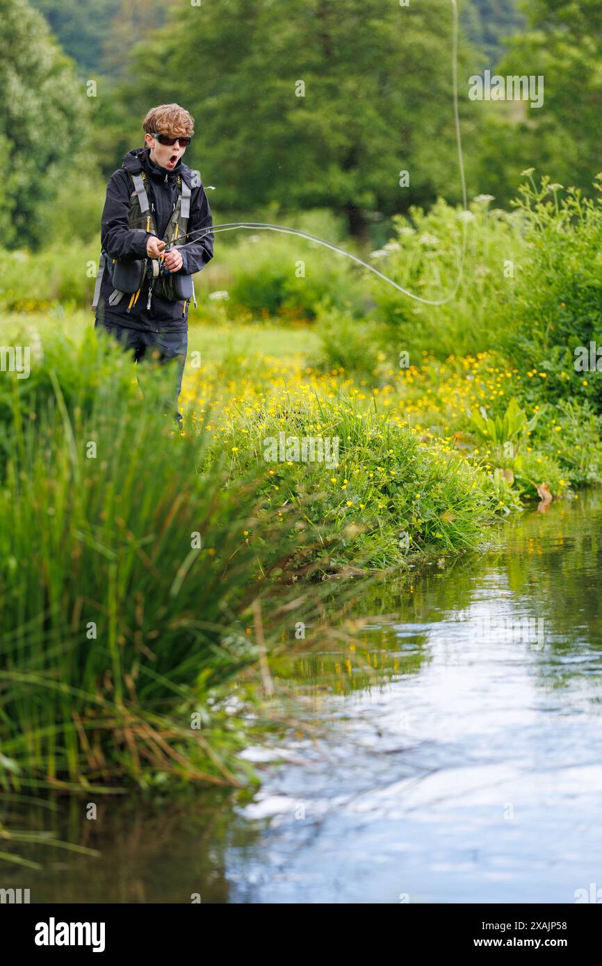 A teenage boy fly fishing for trout on a riverbank in Devon, England in ...