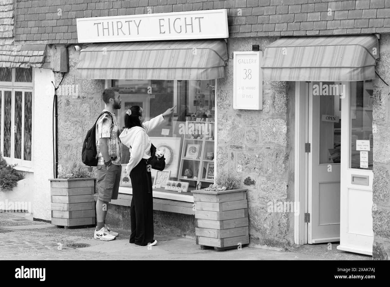 Couple looking in gallery Thirty Eight window in St Ives with tiny dog ...