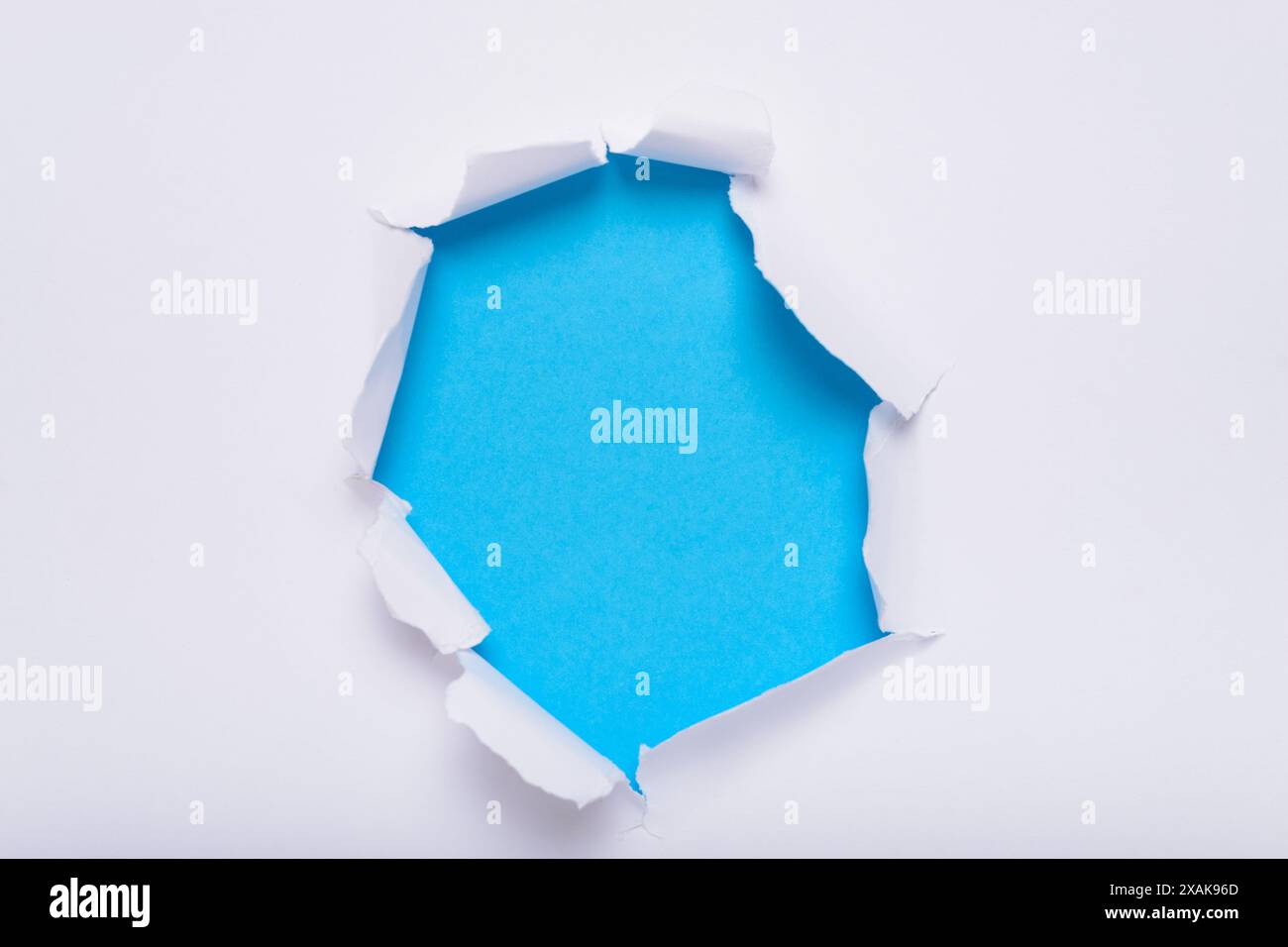 Center torn hole in white paper revealing a blue background. Space for ...