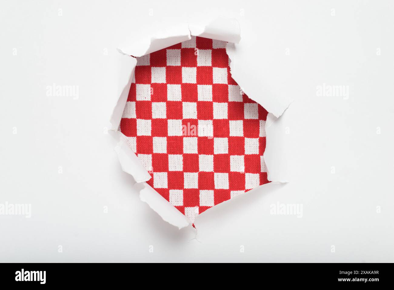 Torn hole in white paper revealing red and white checkered textile ...