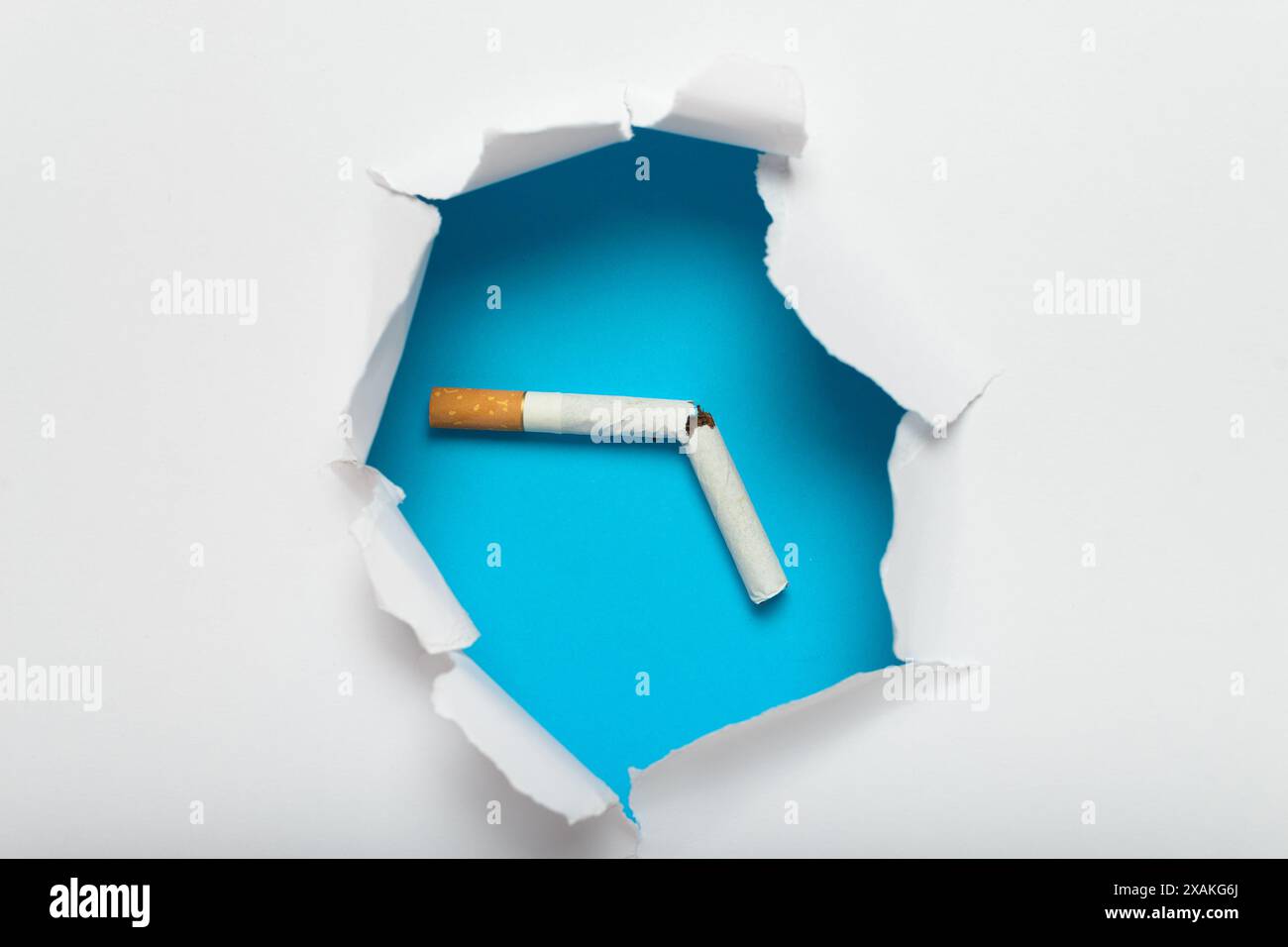 Ripped hole on white paper revealing a cigarette or a cigarette on blue ...