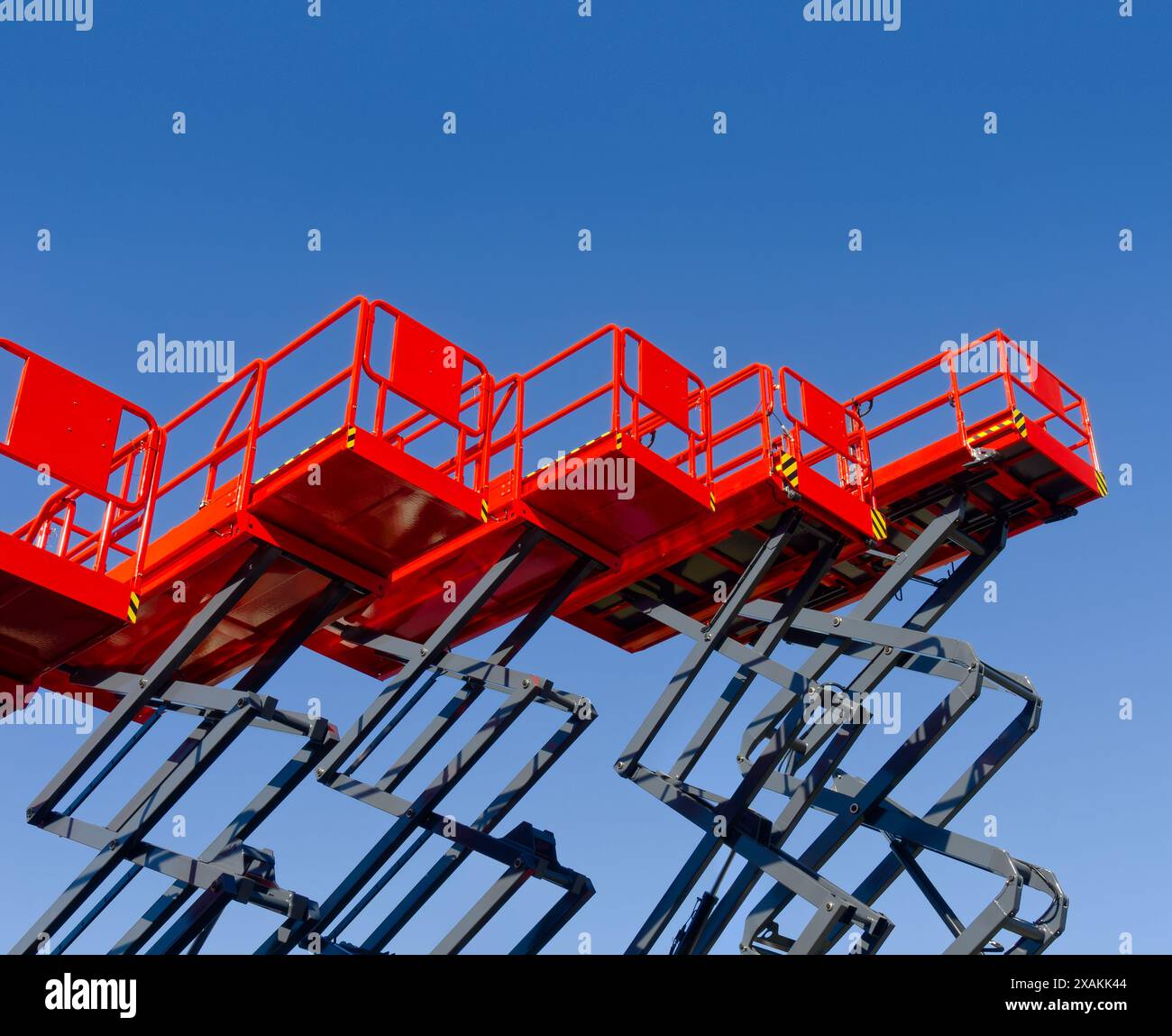 Group of red scissor lifts on a clear blue sky background, low angle ...