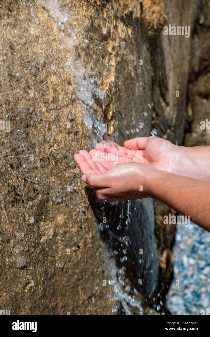 Hands together, in the foreground, taking water from a small waterfall ...