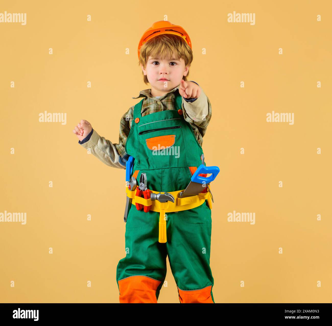 Cute boy in orange hard hat, builder's uniform and tool belt pointing ...