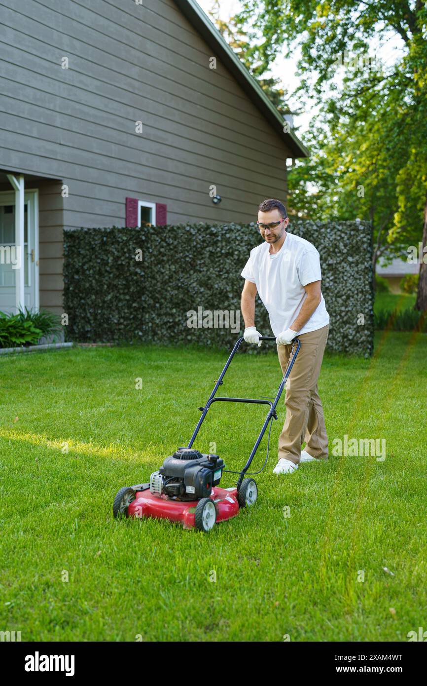 Lawn care. Mowing grass with an electric lawn mower. A young man mows ...