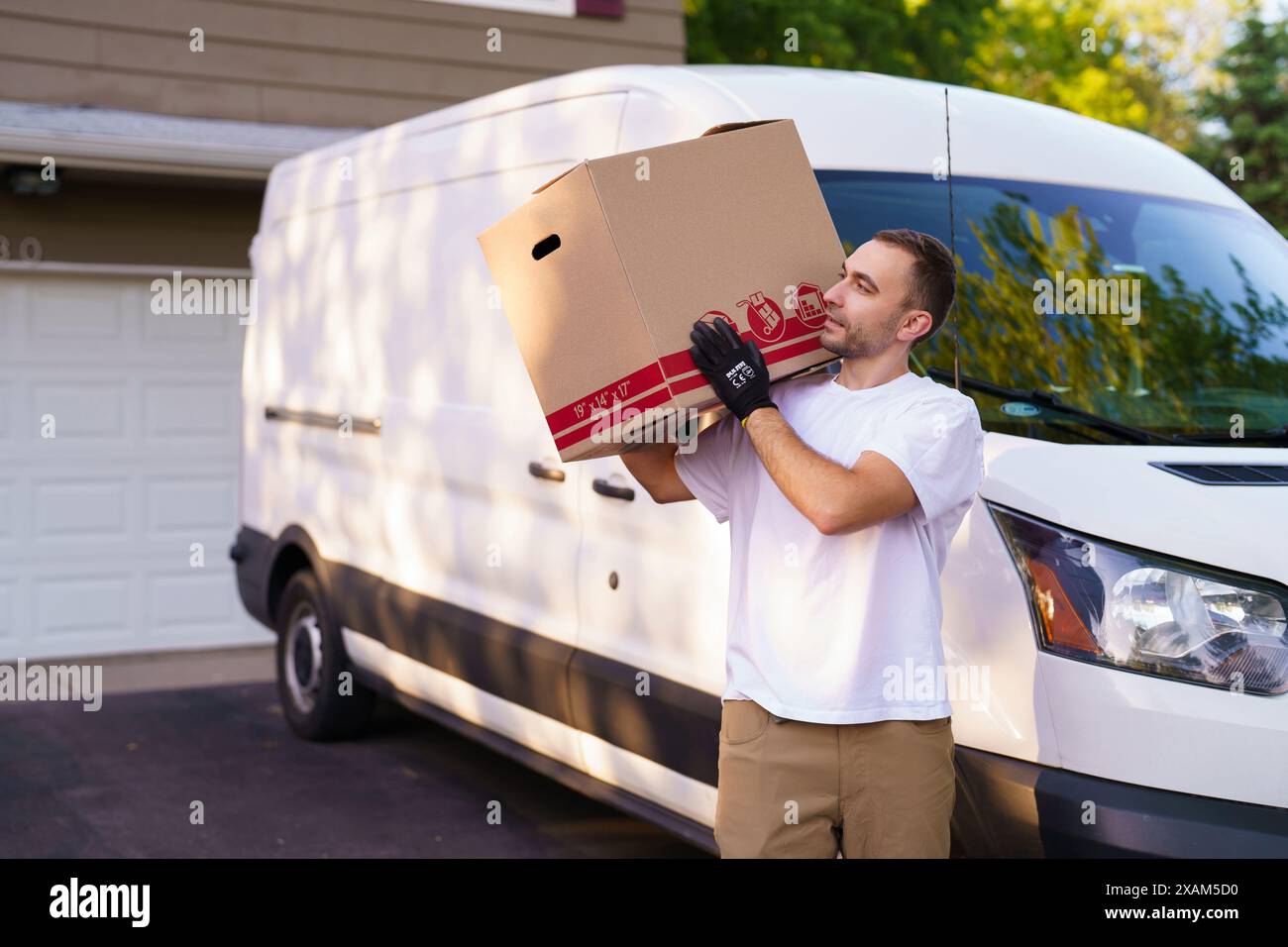Delivery driver smiling at camera holding box in a large warehouse ...