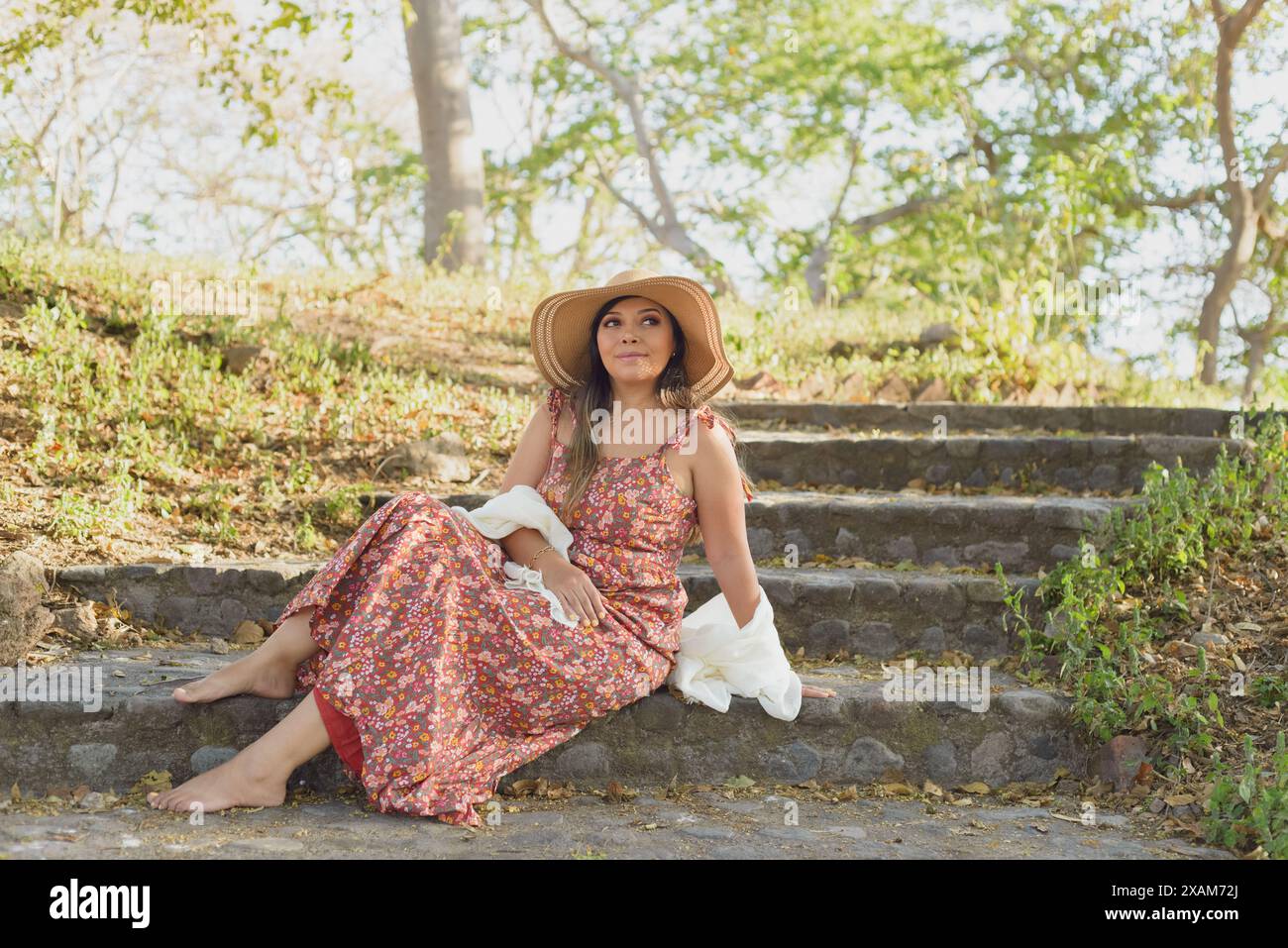 Barefoot woman enjoying nature, seated on the steps of a public garden ...