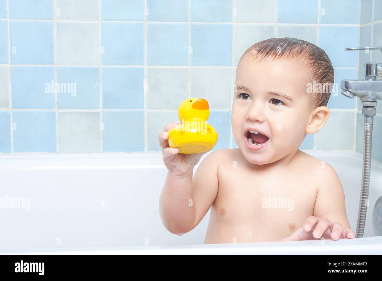 Toddler holds rubber ducky in bathtub. The baby smiles and makes a funny face. Toys and Fun in ...