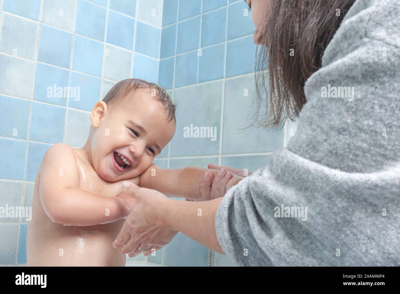 A woman washes a smiling toddler in the bathtub, holding its hand and ...