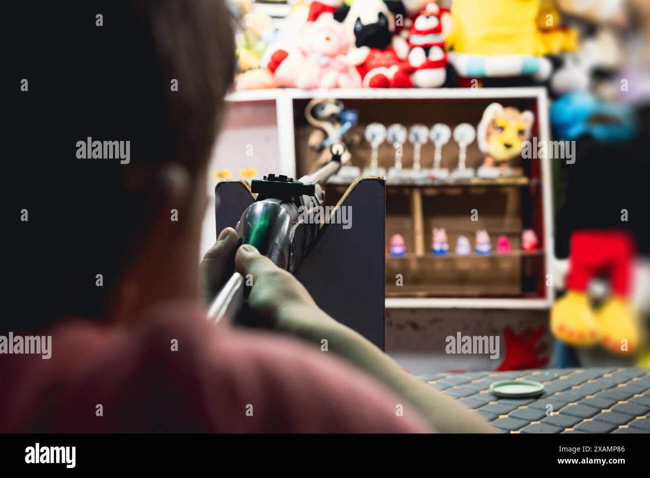 A young boy aiming a rifle at a target in a shooting game booth. The ...