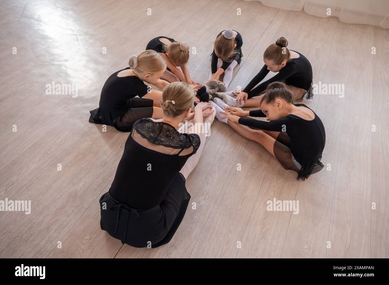 Caucasian woman and five little girls sit in a circle and do stretching ...