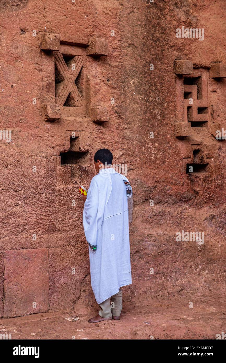 Man in white cloak praying at the walls of rock hewn monolithic ortodox ...