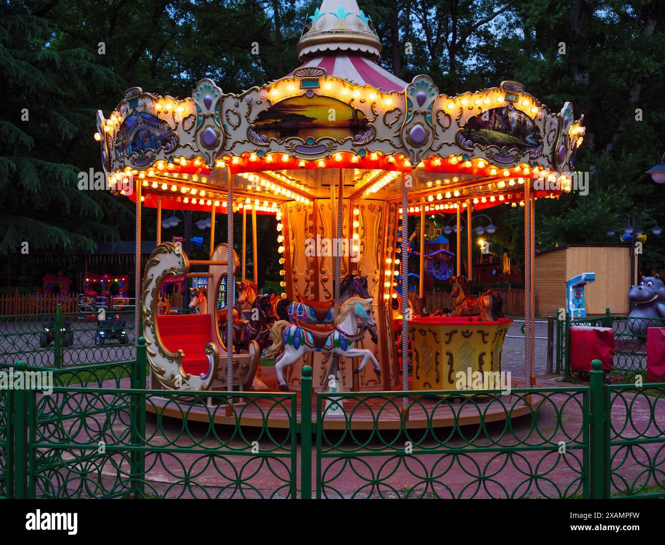 A brightly lit carousel with horses sits in an amusement park at night ...