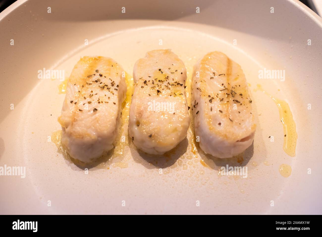 Top view of Three fresh hake loins are cooked in a white granite pan ...
