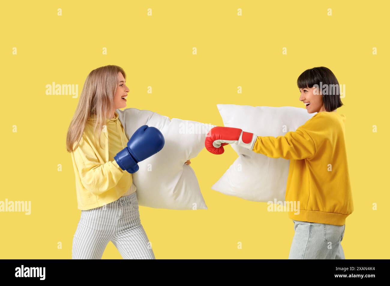 Young women in boxing gloves fighting pillows on yellow background ...