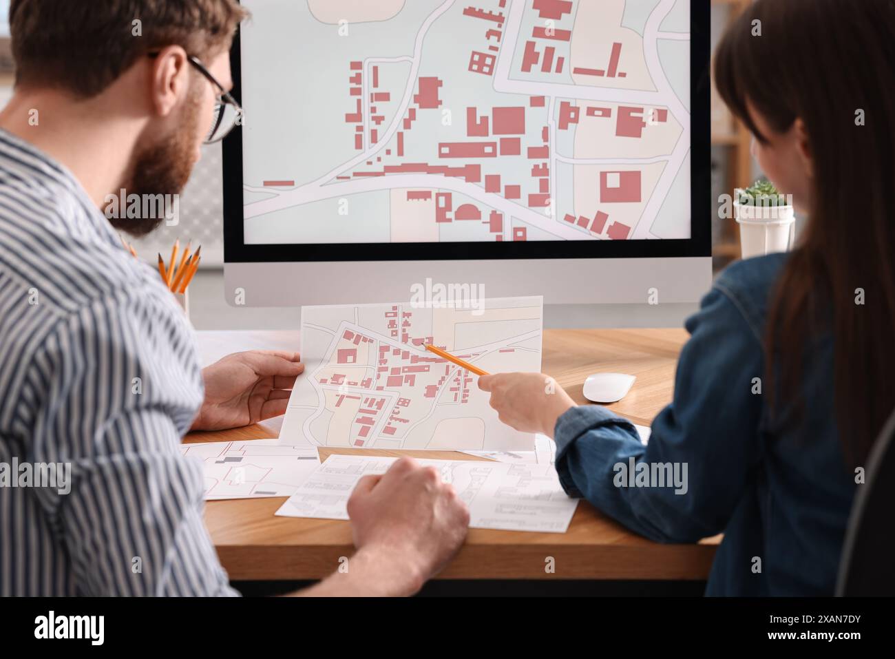 Cartographers working with cadastral maps at table in office, back view ...