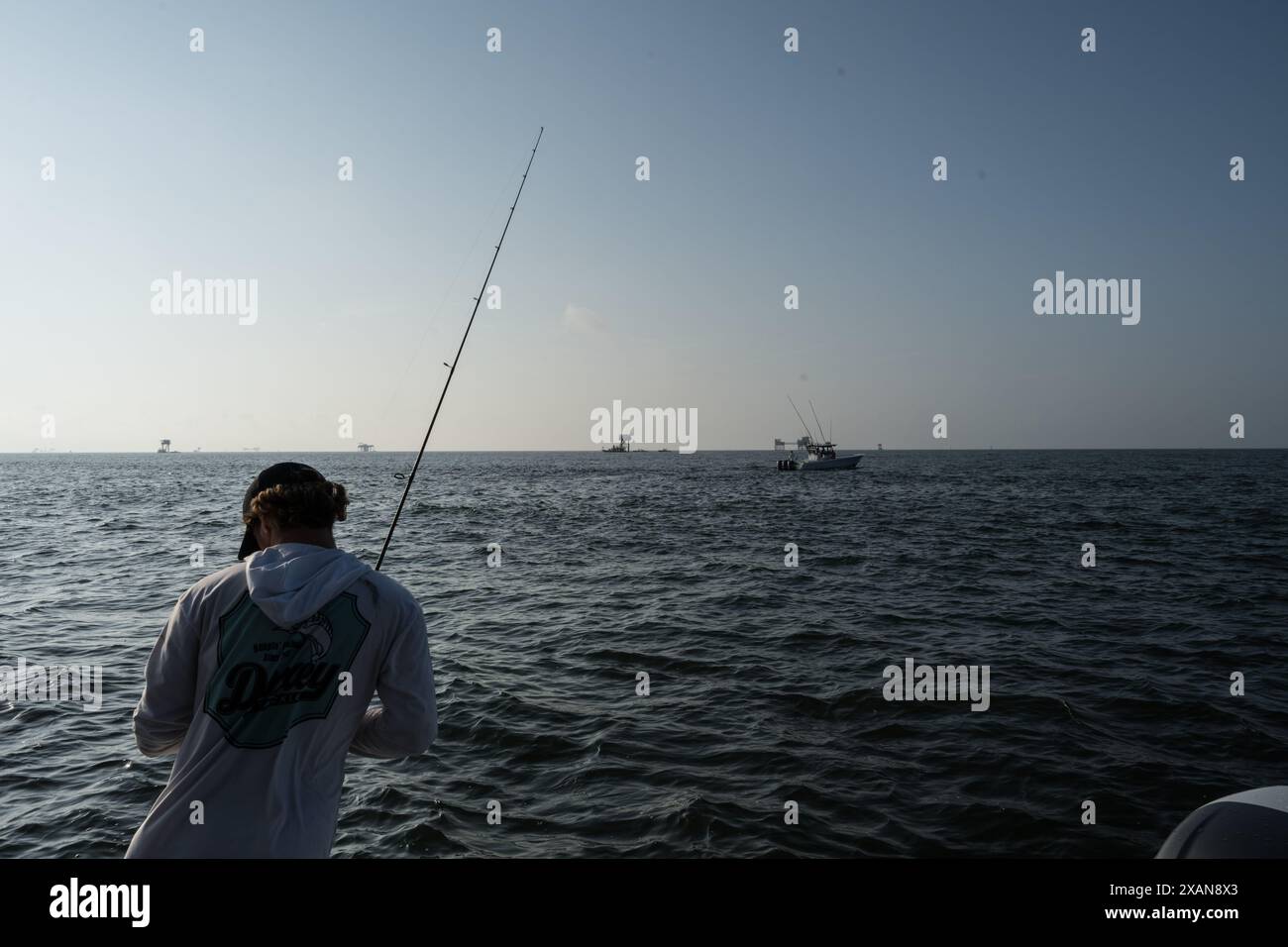 An angler fishes for baitfish while surrounded by offshore oil ...