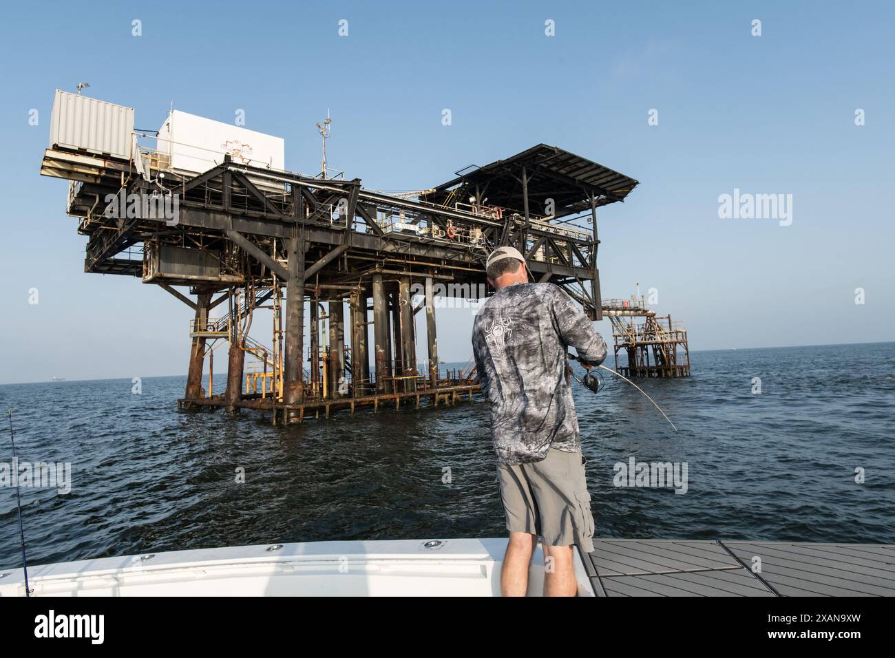 An angler fishes for baitfish while surrounded by offshore oil ...
