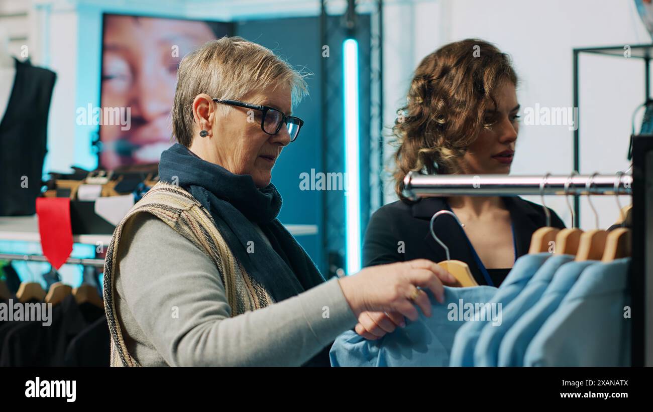 Retail worker suggesting fashion items to elderly customer in clothing ...