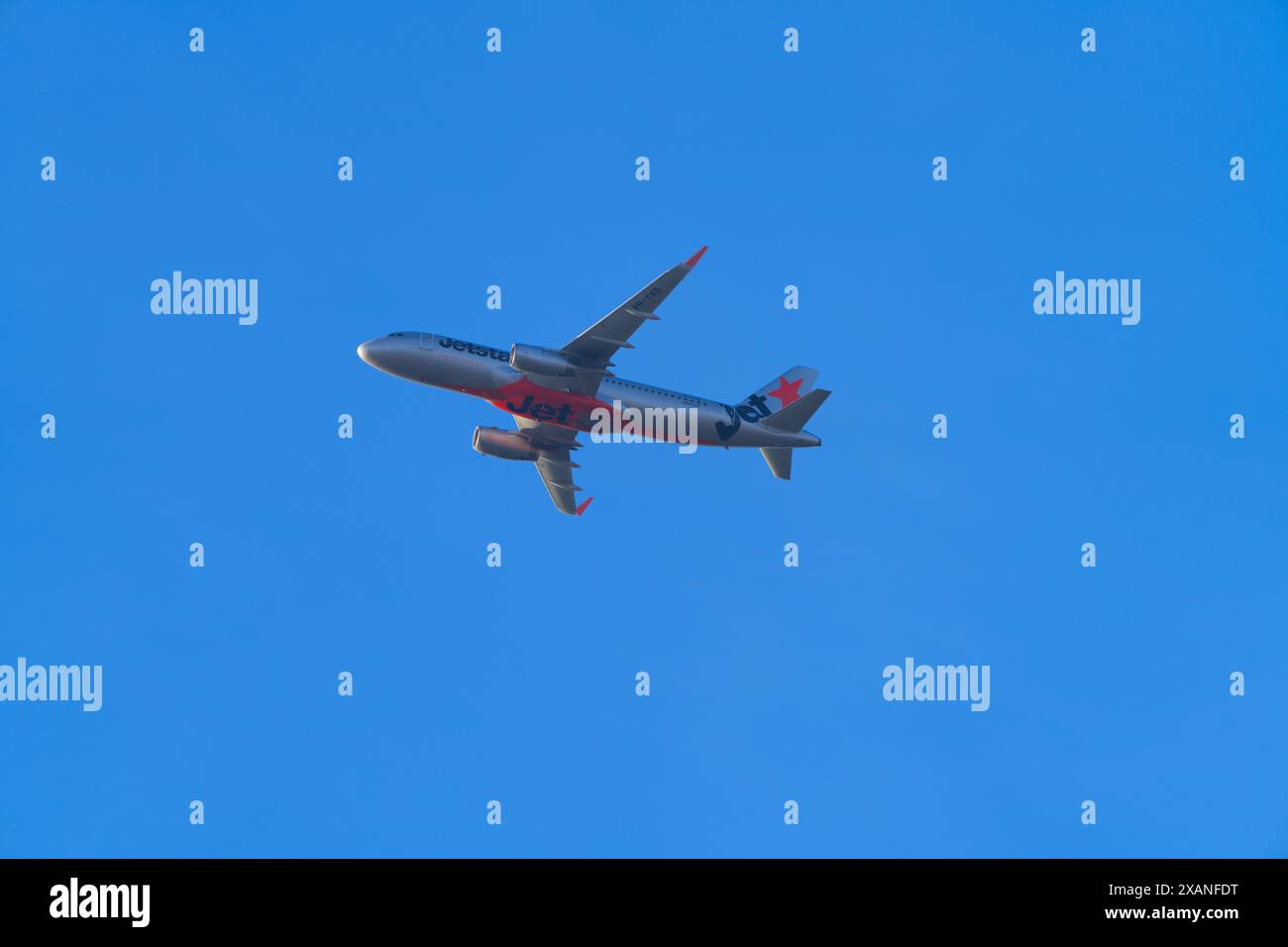 A Jetstar jet plane in flight with a cloudless blue sky background ...