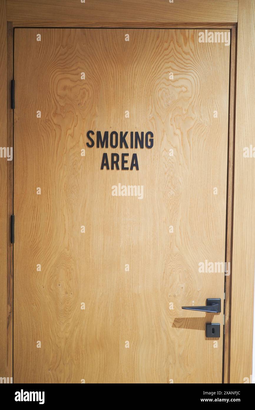 A designated smoking area sign is displayed on a wooden door in a ...