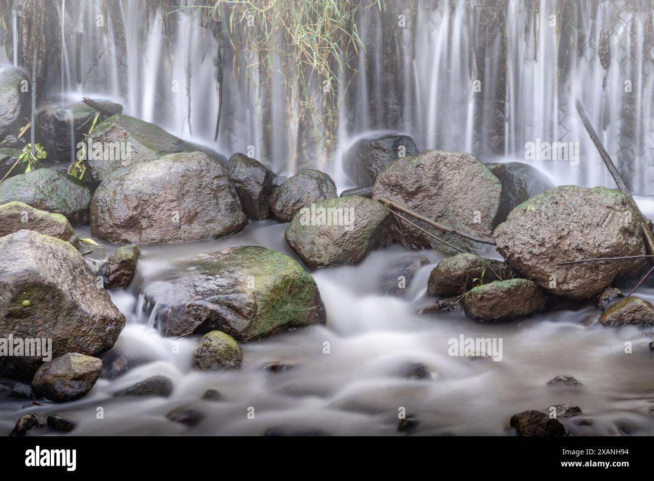 A stream of water flows over a rocky bank. The water is murky and the ...