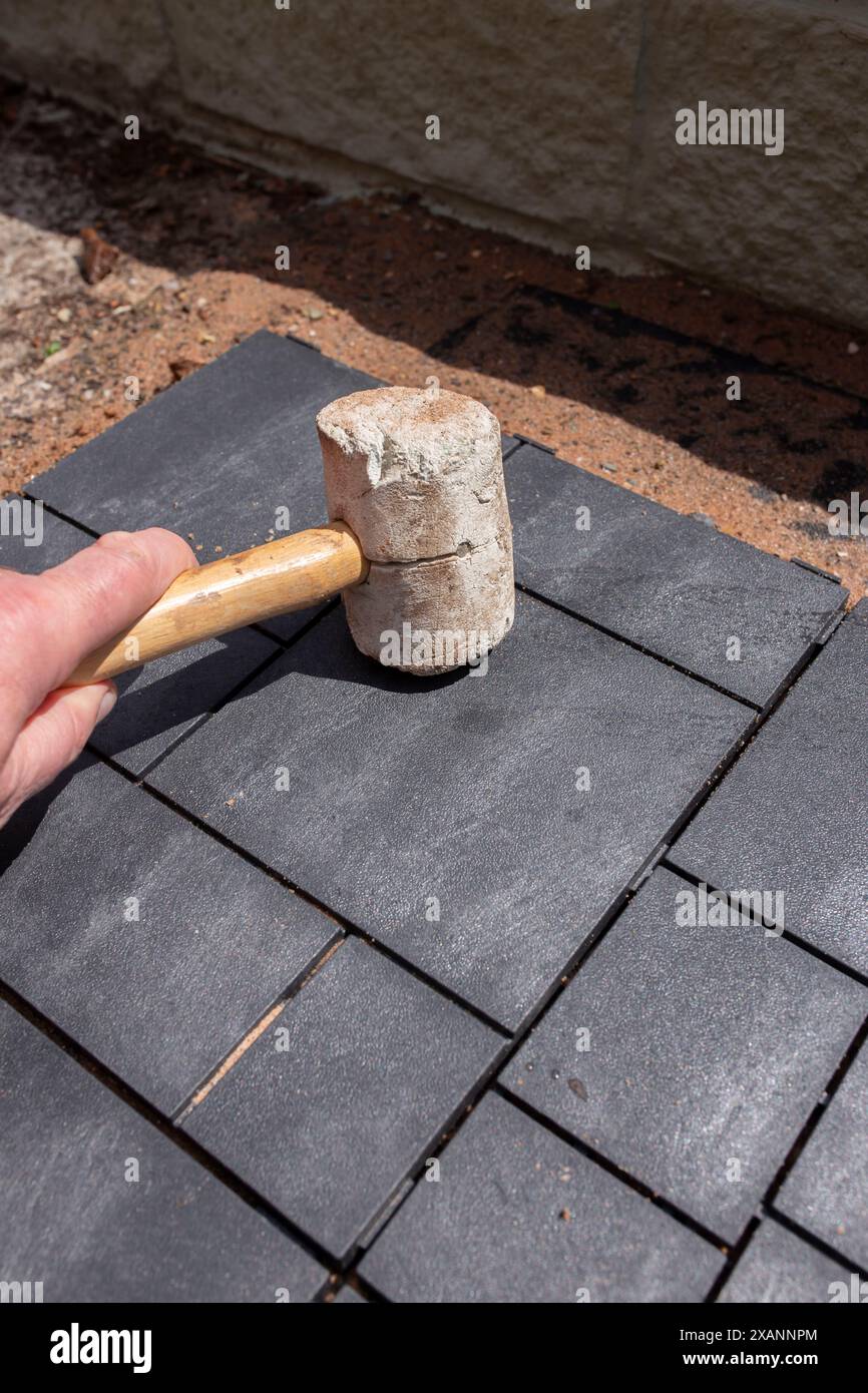 Man laying composite decking tile patio with a rubber mallet. Garden ...