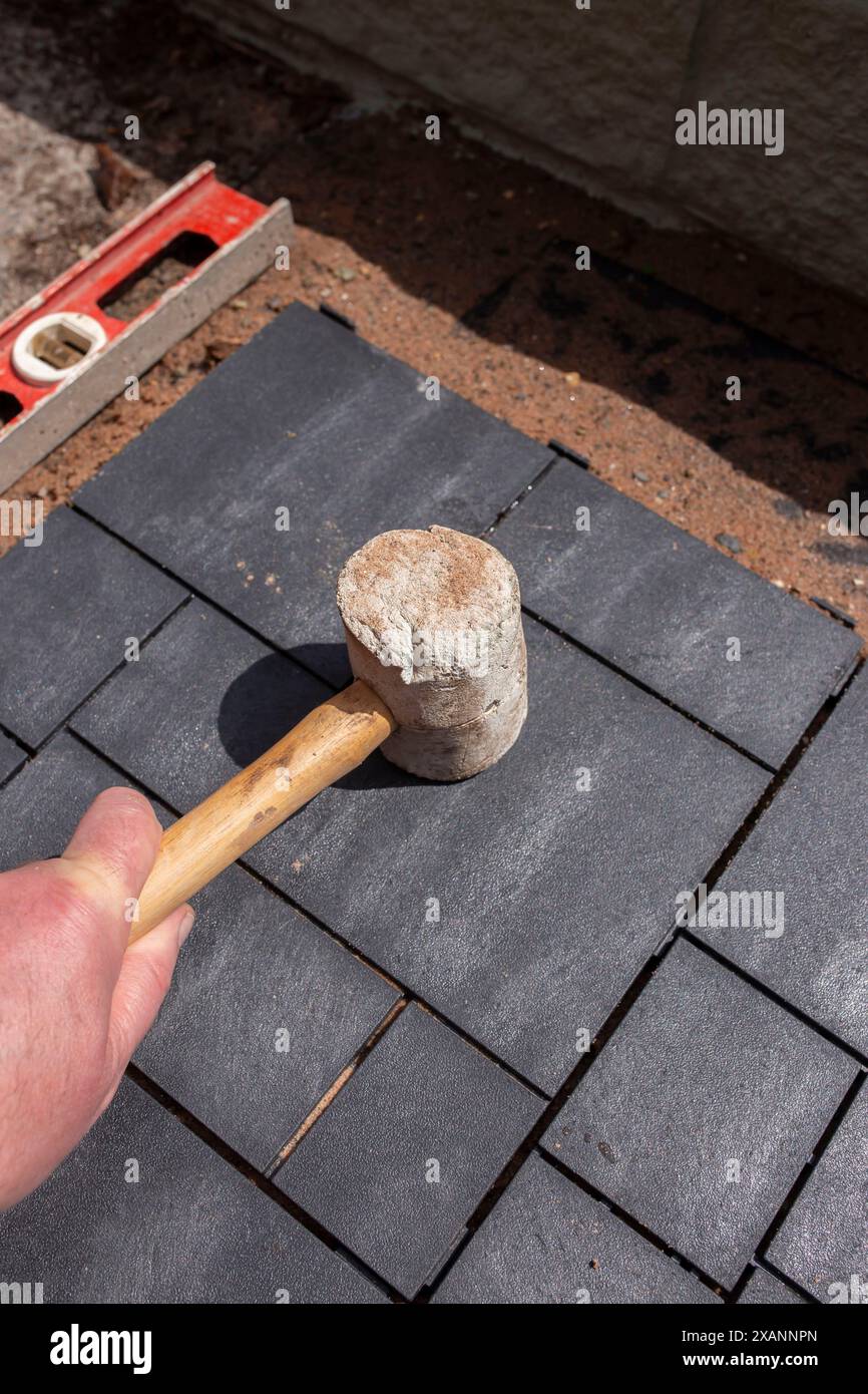 Man laying composite decking tile patio with a rubber mallet. Garden ...