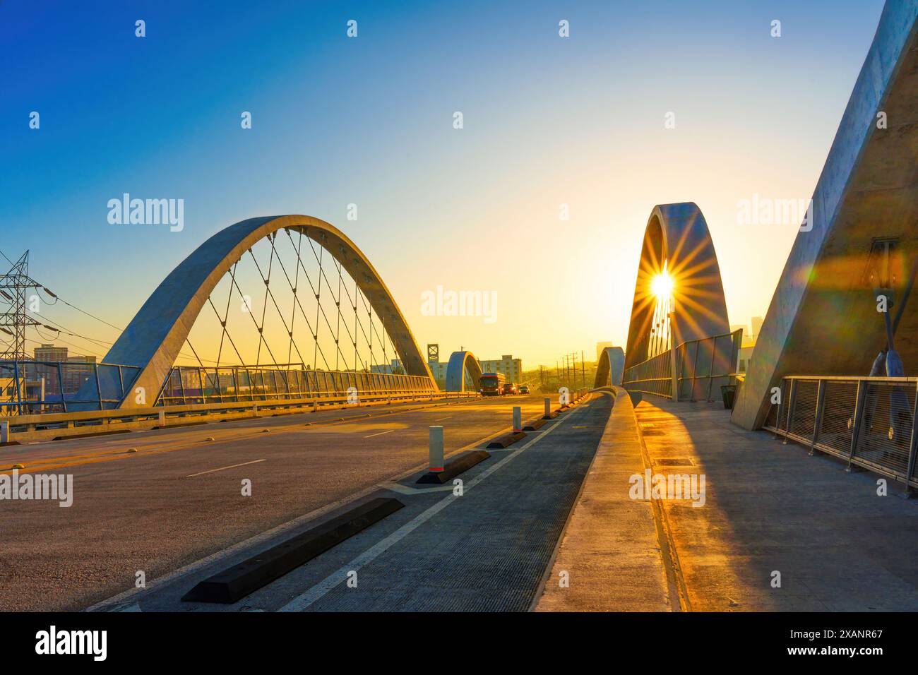 Modern arch bridge captured during sunset, with warm sunlight peeking ...