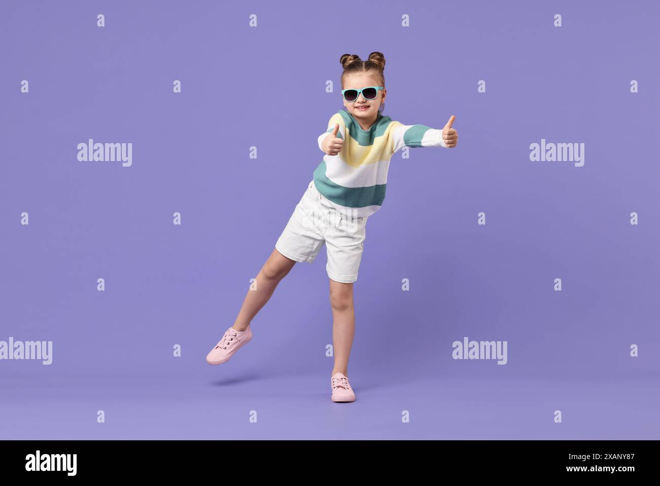Cute little girl in sunglasses showing thumbs up while dancing on ...