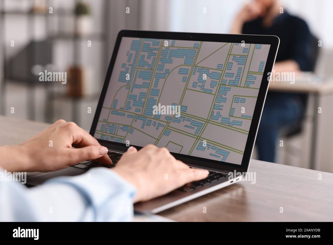 Smiling cartographer working with cadastral map on laptop at wooden ...