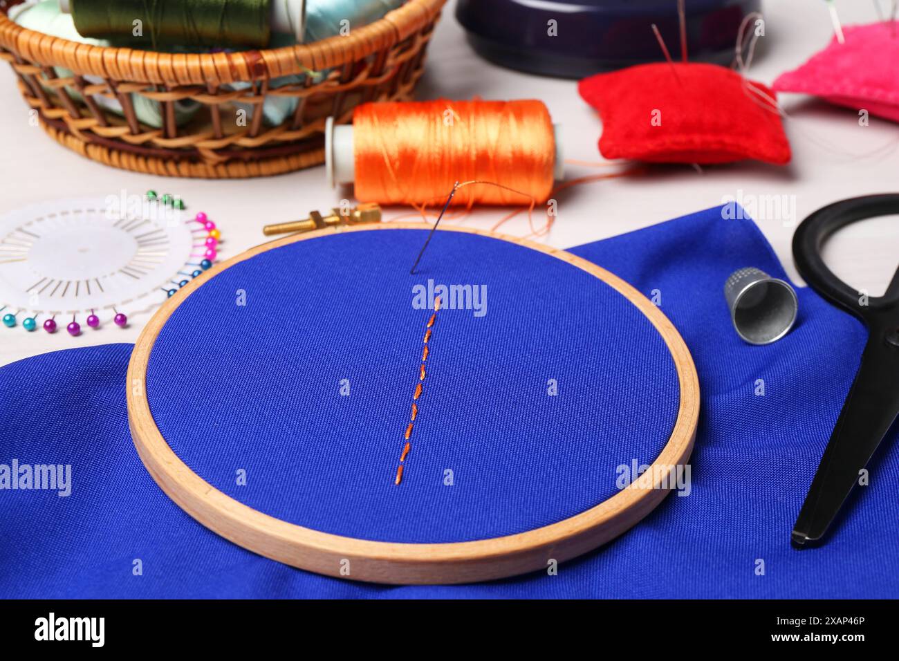 Blue cloth with stitches, sewing thread, needle and scissors on light ...