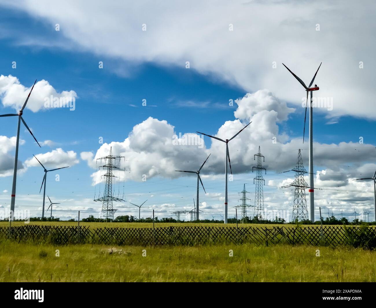 Wind Turbines And Electricity Pylons With Cables In Front Of Cloudy Sky ...